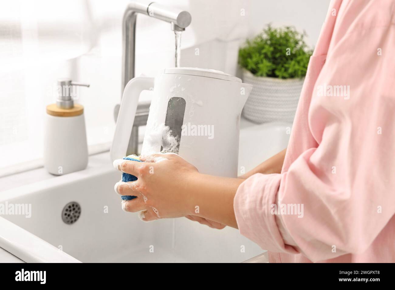 Woman washing electric kettle with sponge at sink in kitchen, closeup ...
