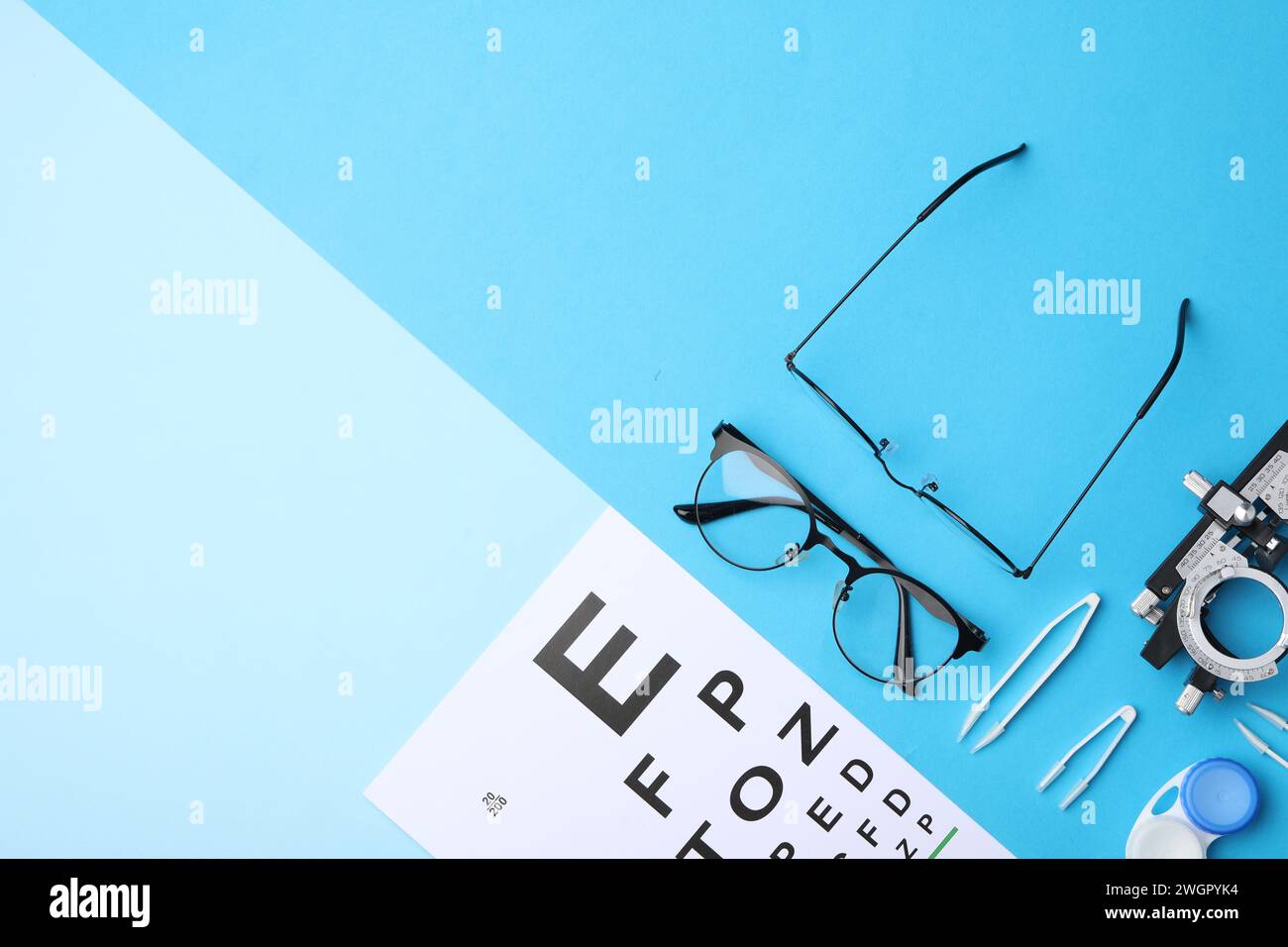Flat lay composition with vision test chart and glasses on light blue ...