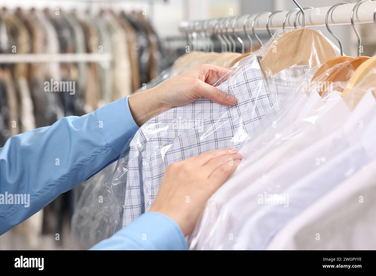 Dry-cleaning service. Woman taking shirt in plastic bag from rack ...