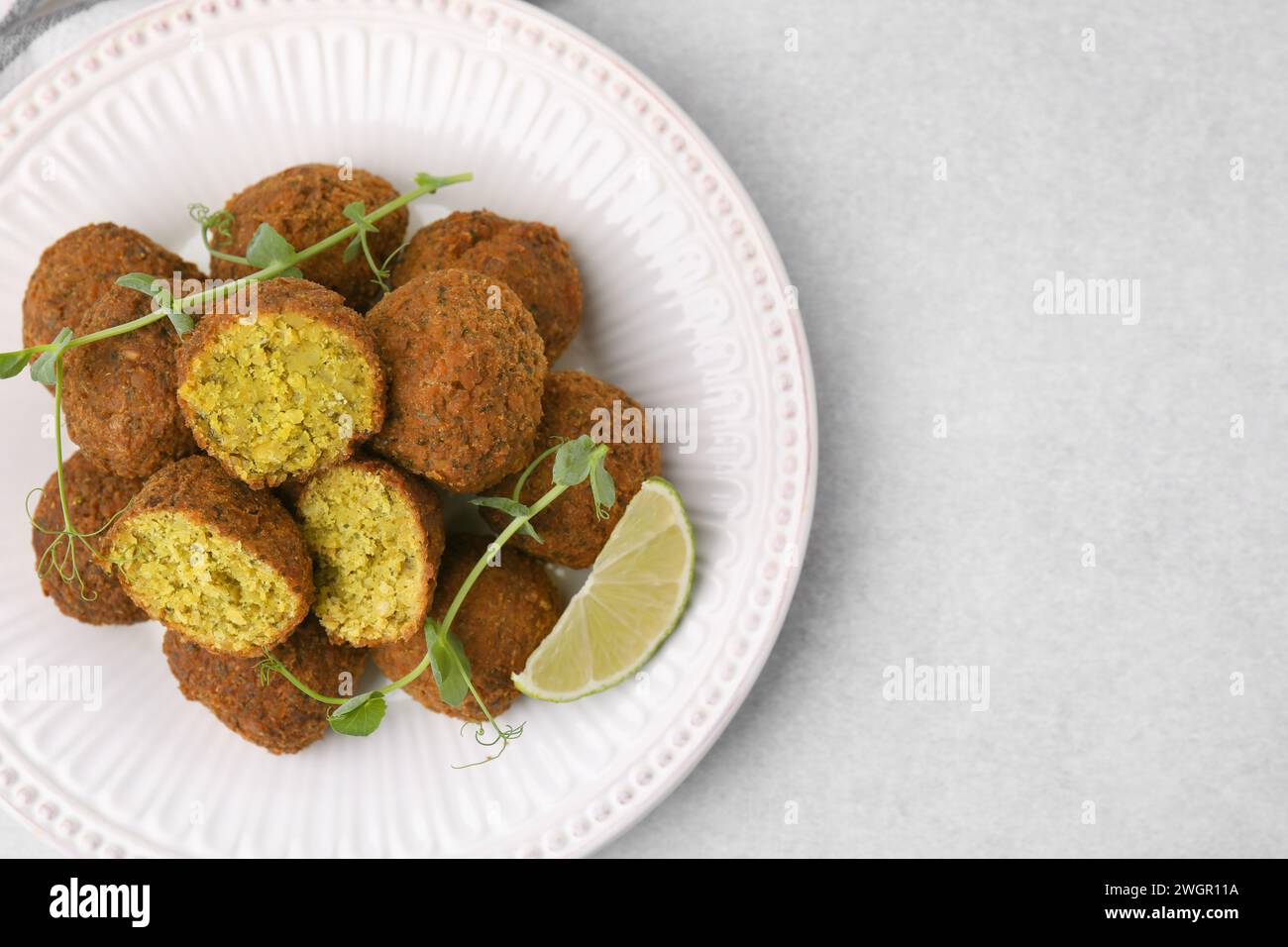 Delicious falafel balls, lime slice and microgreens on light table, top ...