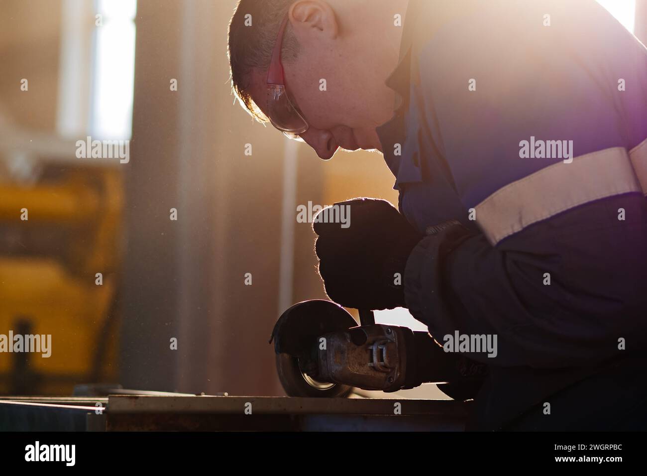 Metal mechanic works with angle grinder in factory workshop. Backlit ...