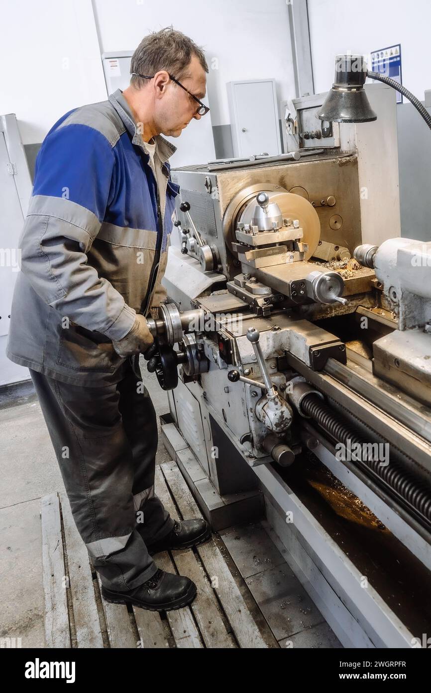 Turner in overalls works at lathe in turning shop at factory. Elderly ...