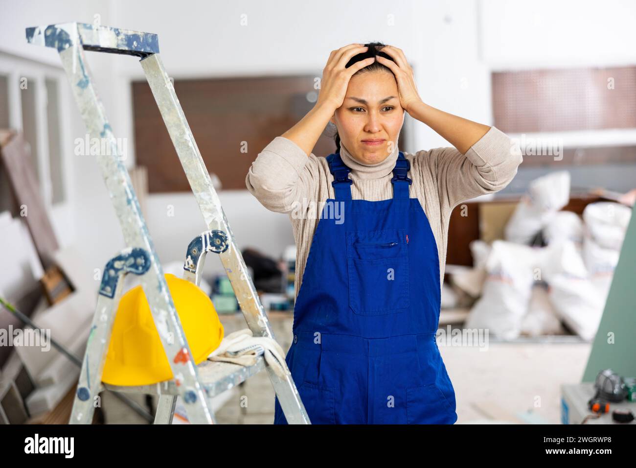 Frustrated woman builder holding head while standing in construction ...