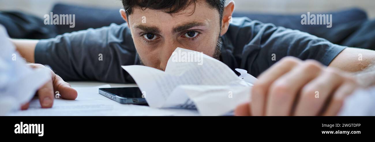 frustrated man sitting at table with papers and phone on it during ...