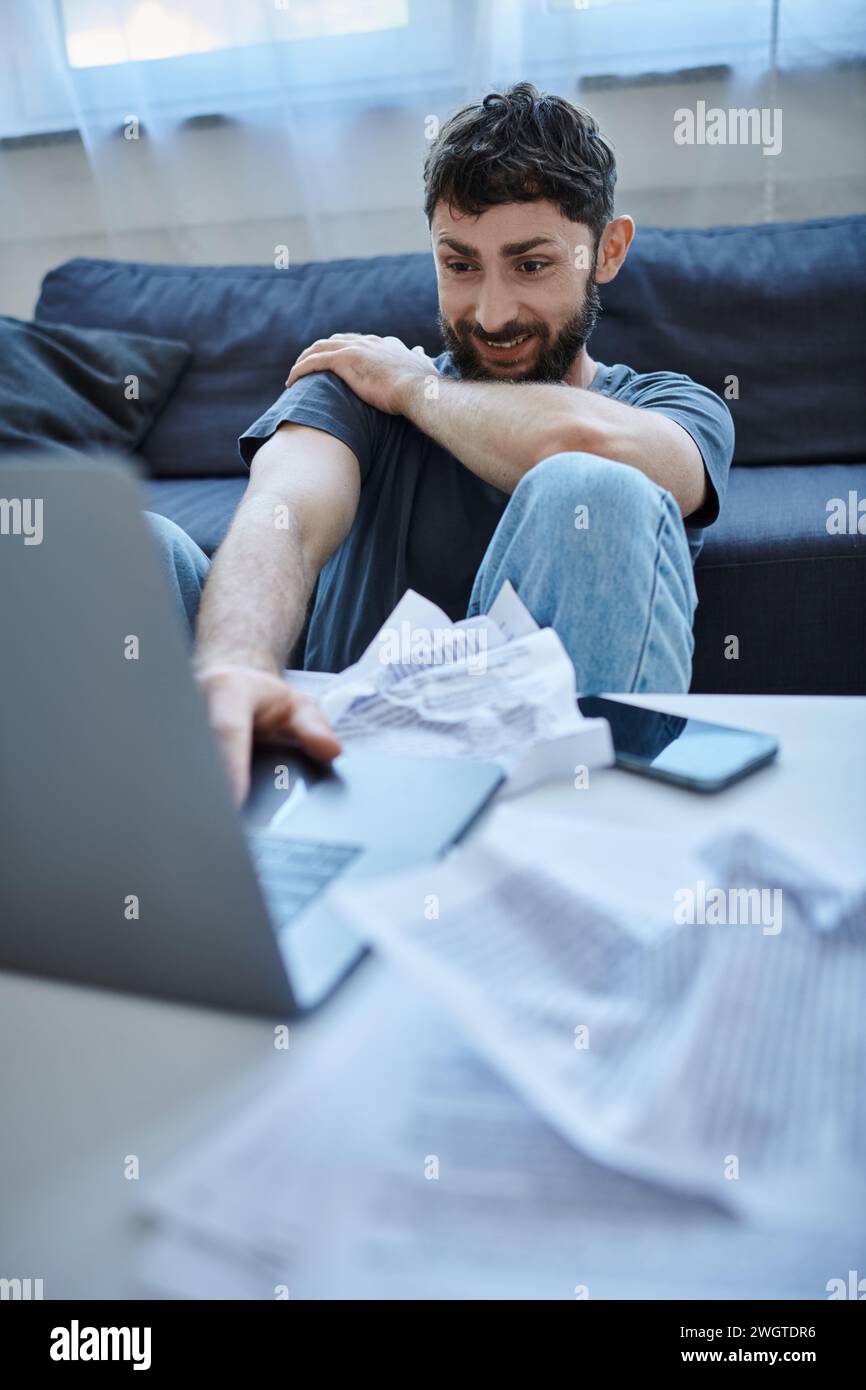 depressed man with crazy smile in homewear looking at his laptop during ...