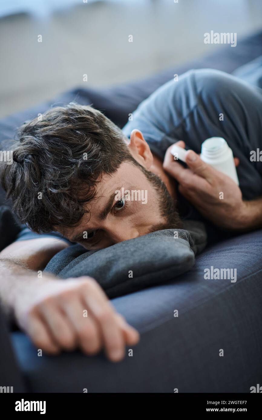 traumatized suffering man with beard lying on sofa with pills in hand ...