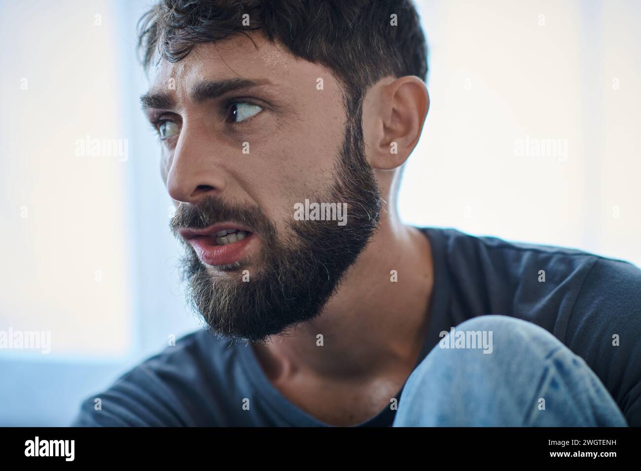 ill traumatized man with beard biting his lips during depressive ...