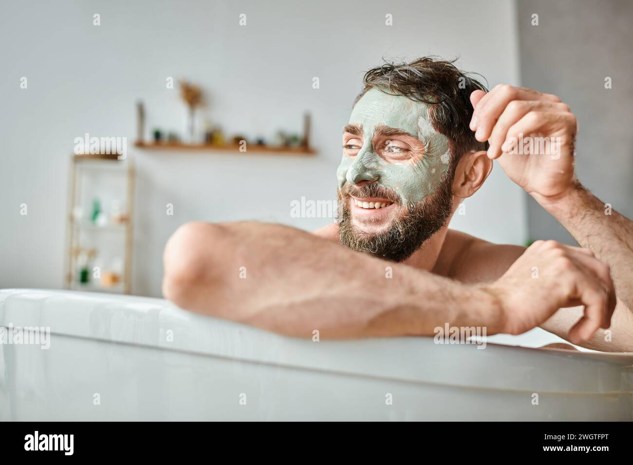 joyful attractive man with beard and face mask chilling in his bathtub ...