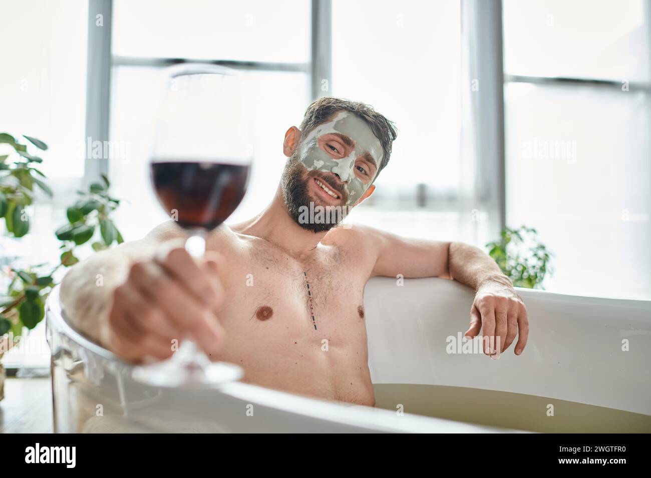 cheerful attractive man with beard and face mask relaxing in bathtub ...