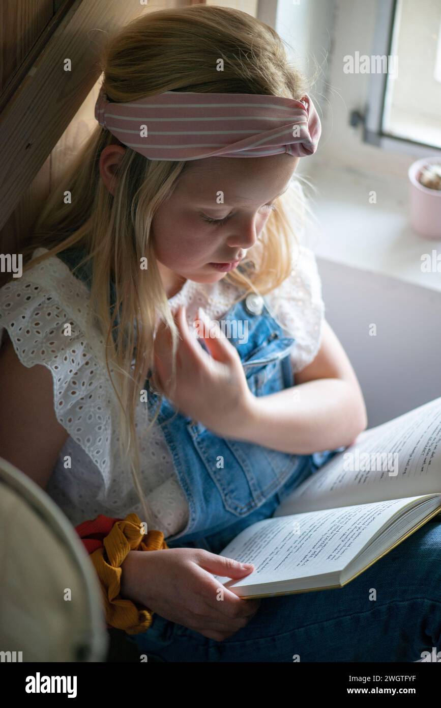 Young girl sitting next to her bedroom window reading her favourite ...