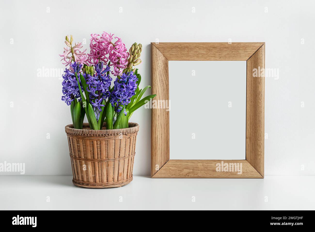 Wooden mock up photo frame and blooming hyacinth on a white table ...