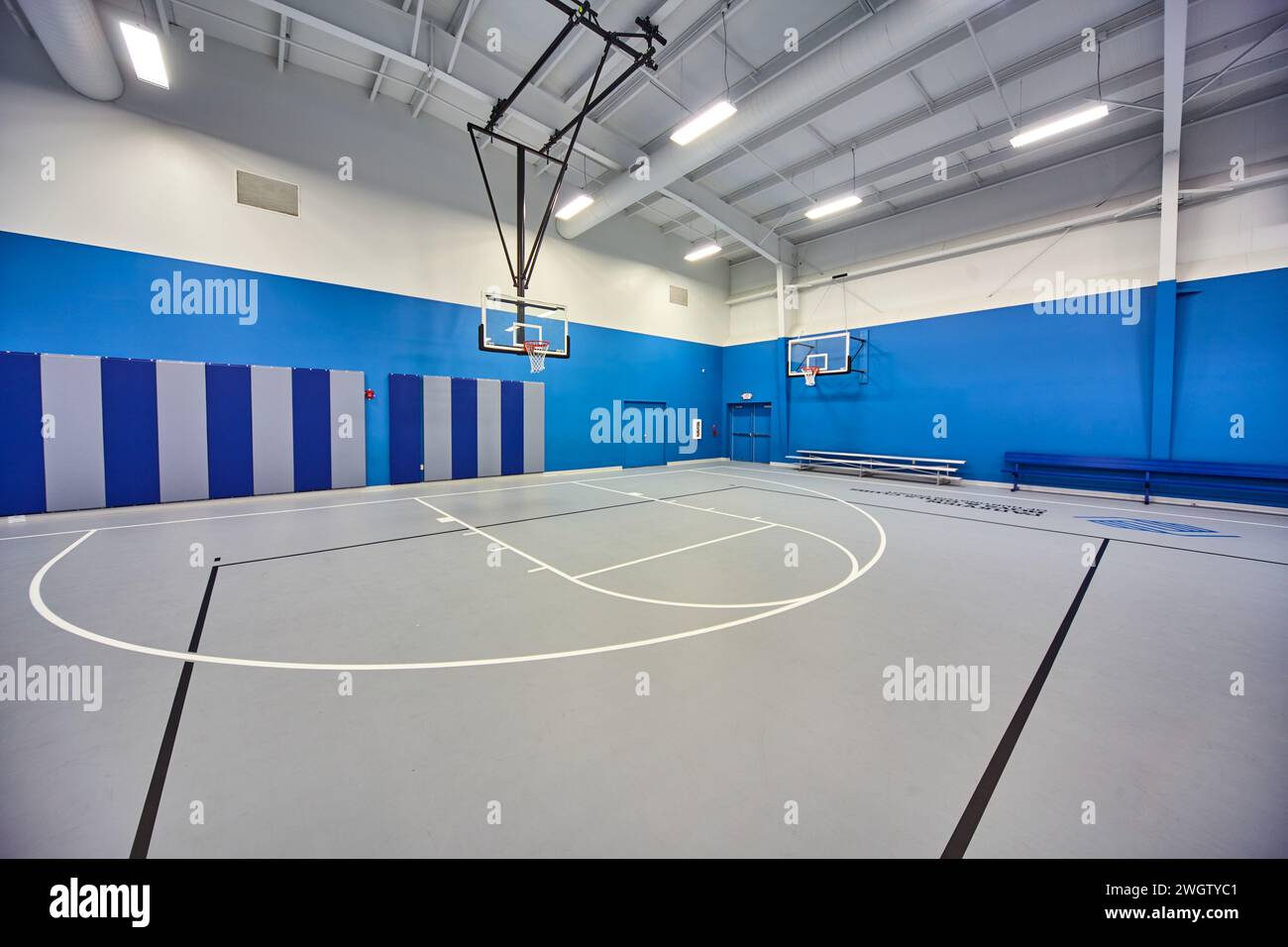 Bright Indoor Basketball Court with Blue Walls and Retracted Bleachers ...