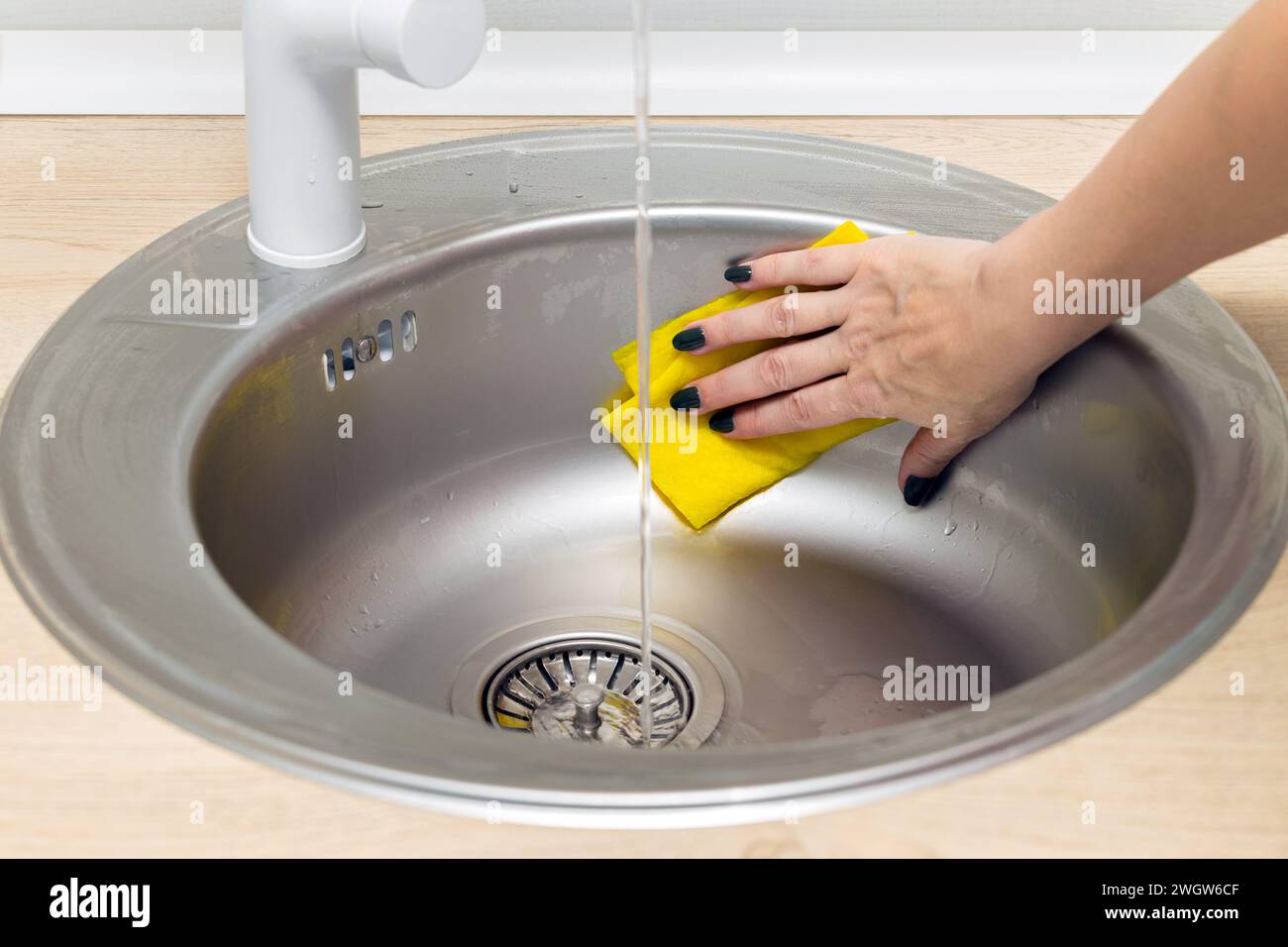 woman washing the sink in the kitchen, close up. hand wipes a stainless ...