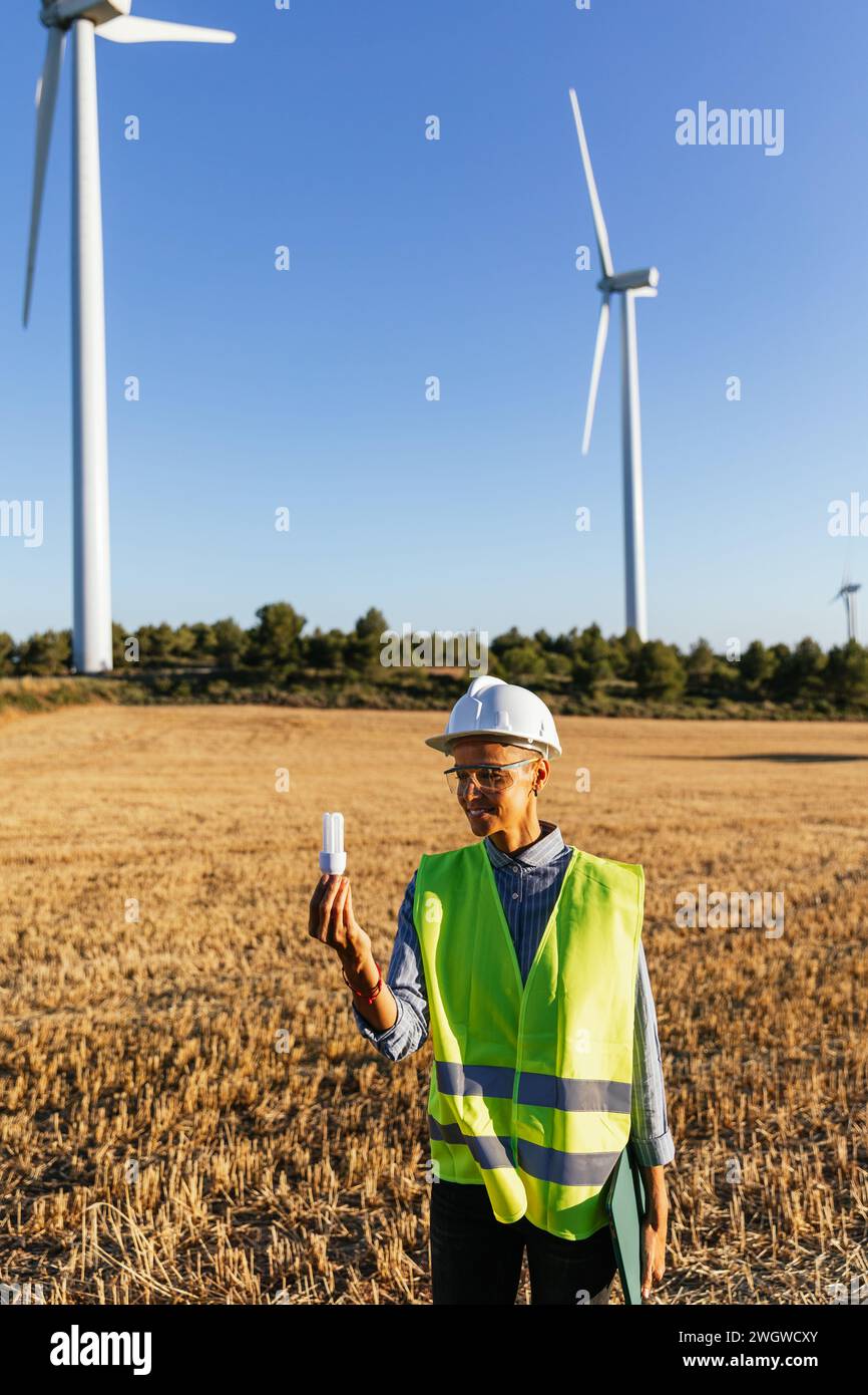 Female engineer holding an energy-saving light bulb against windmills ...