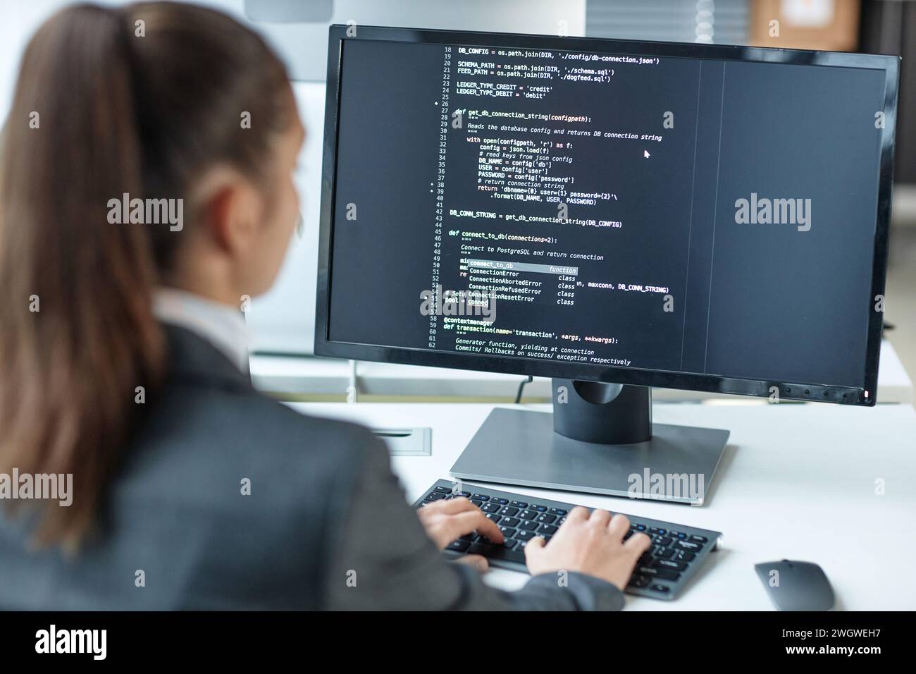 Over shoulder view of female programmer using computer with code lines on screen in IT company ...