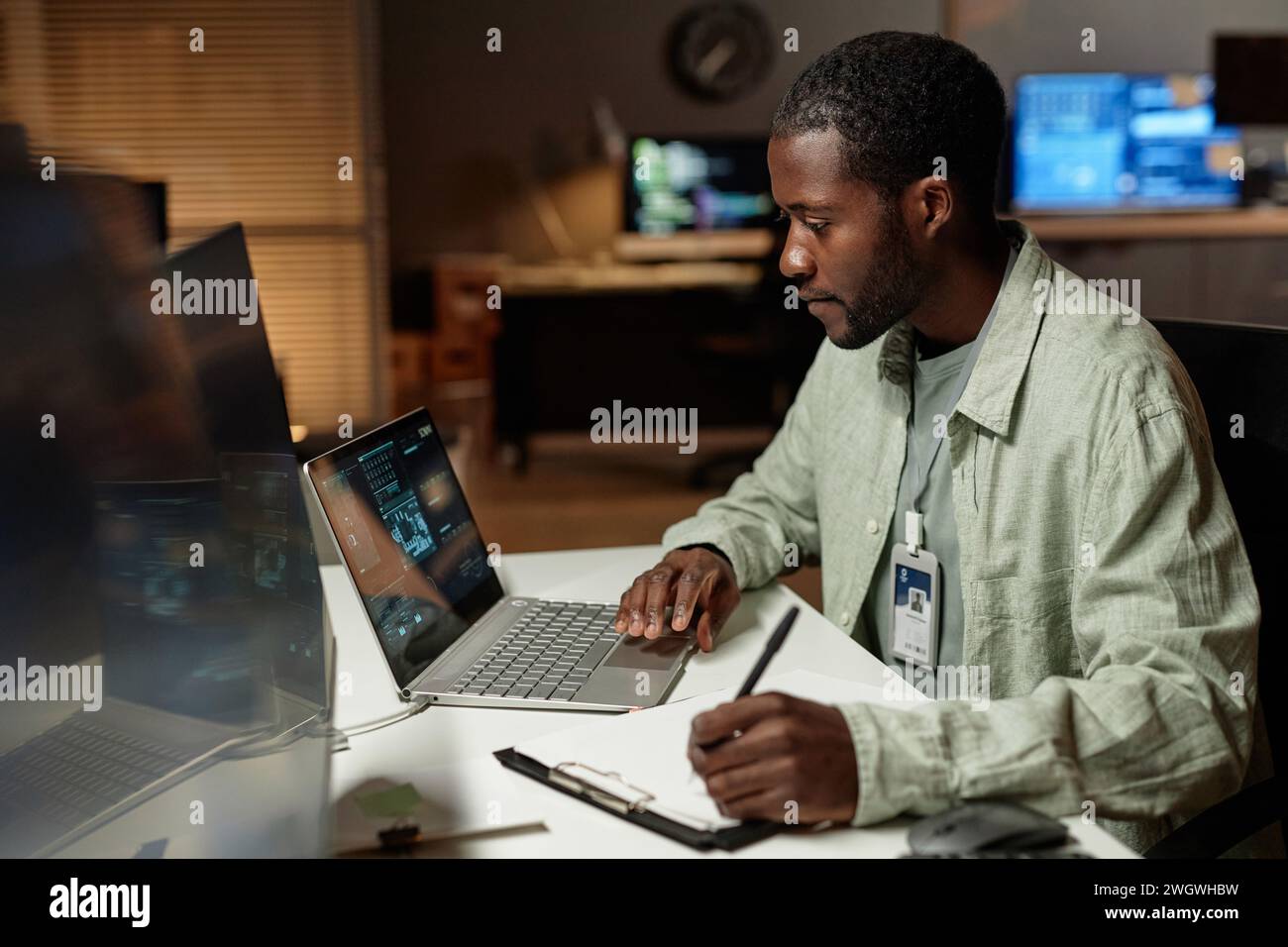 Side view portrait of Black young man using computer and taking notes ...