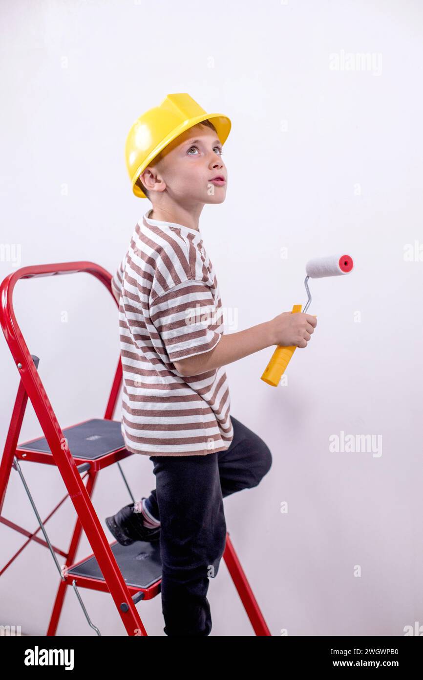 A child builder stands on a ladder and paints white walls in an ...