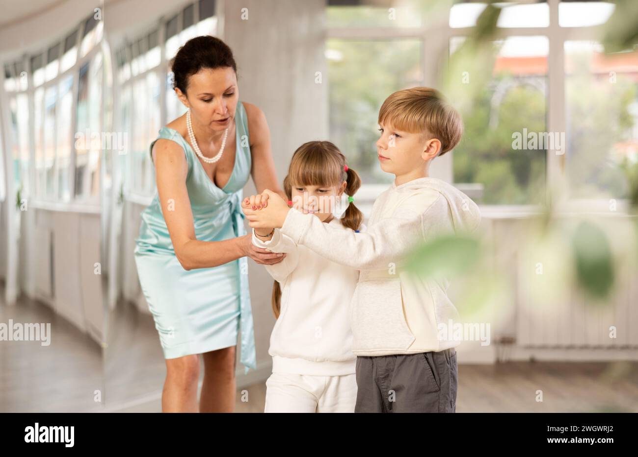 Female instructor adjusting ballroom dance stance of preteen dancers ...