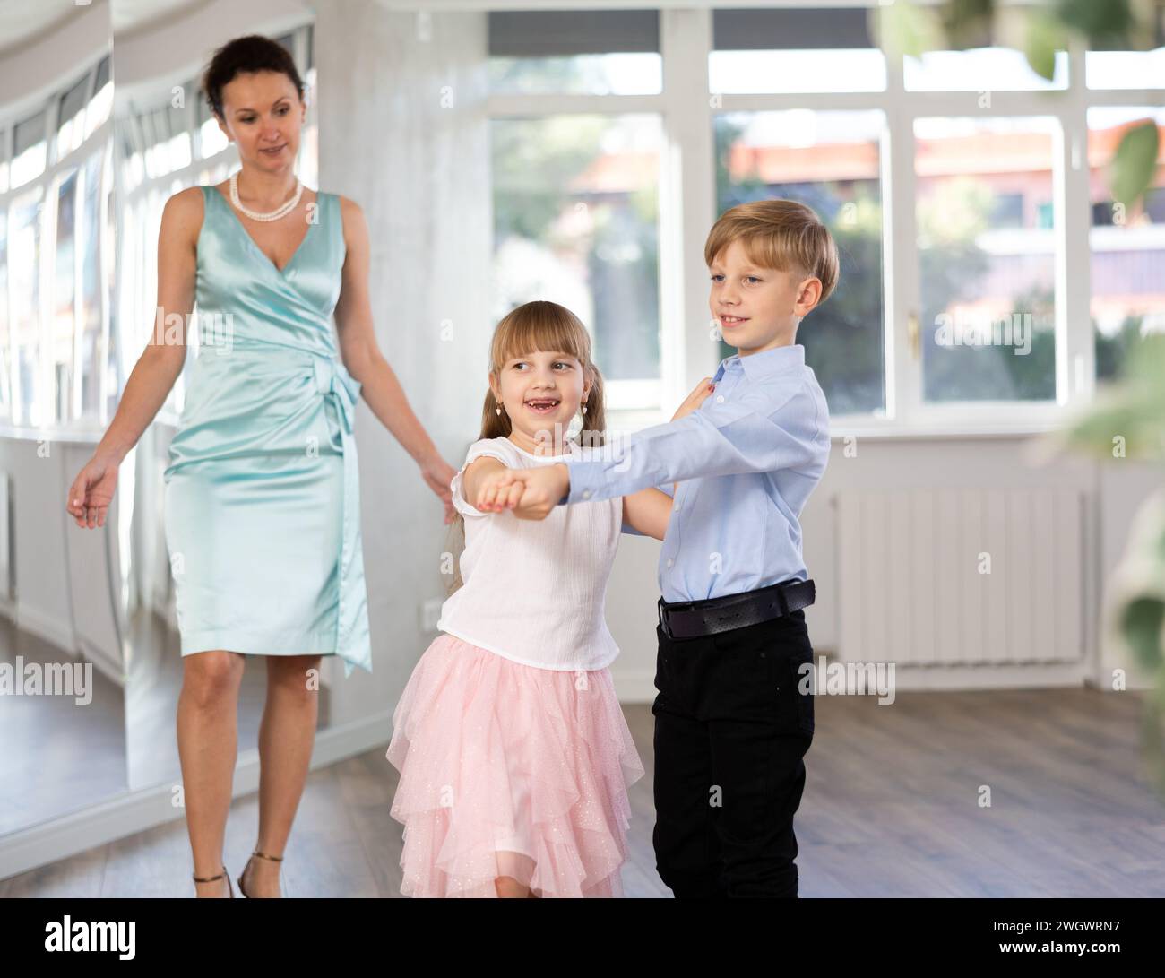 Tween girl and boy practicing waltz in dance hall with female mentor ...