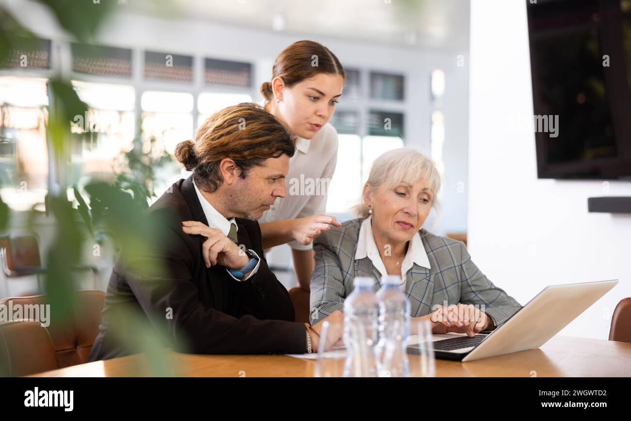 three positive office workers are sitting at table animatedly and ...