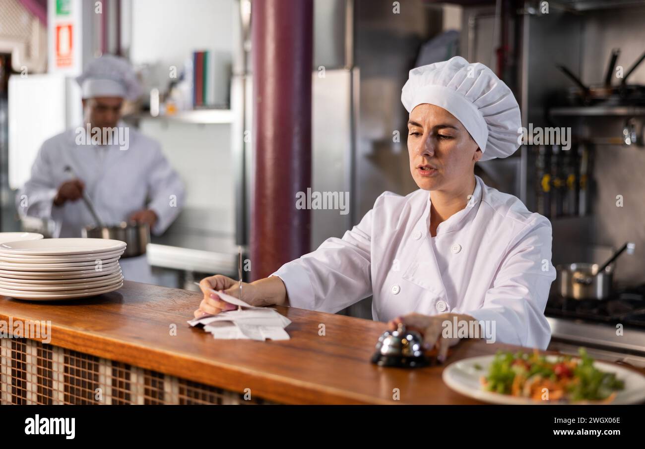 Female cook reads the paid check and presses the bell for the waiter in ...
