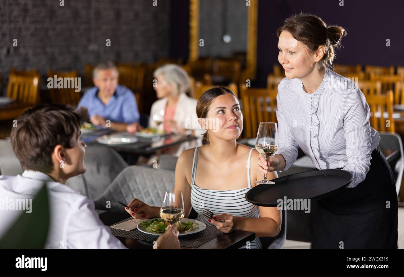 Waitress serves order of wine and wishes visitors young couple pleasant ...