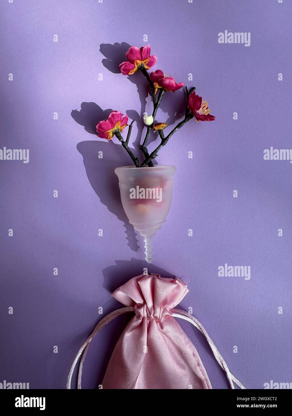 Menstrual cup with red flowers and pink silk bag, flat lay on purple ...