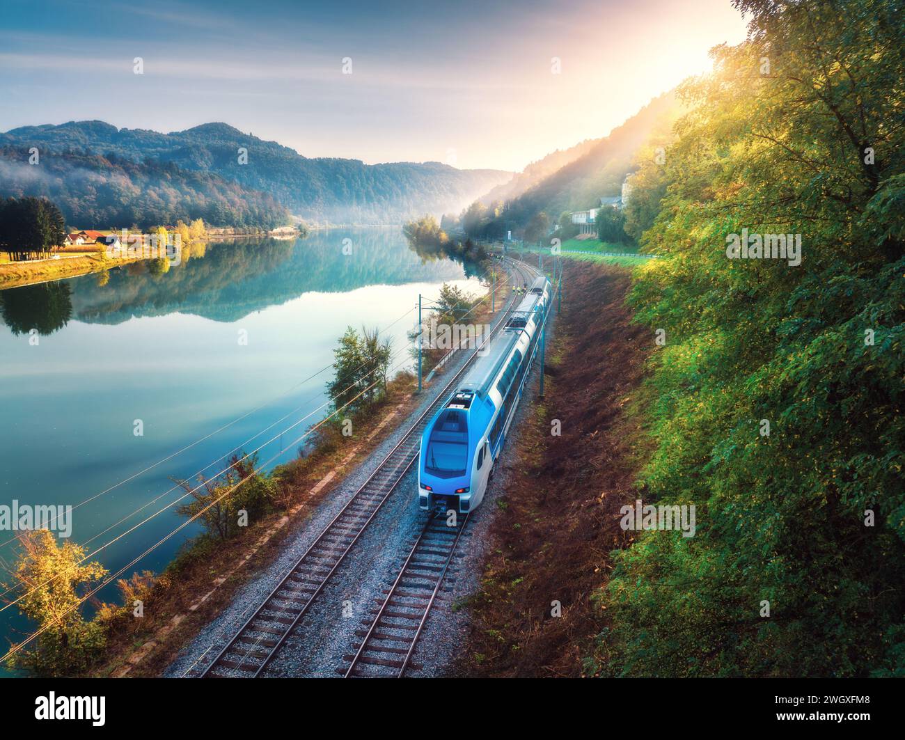 Aerial view of blue train near river in mountains at sunrise Stock ...