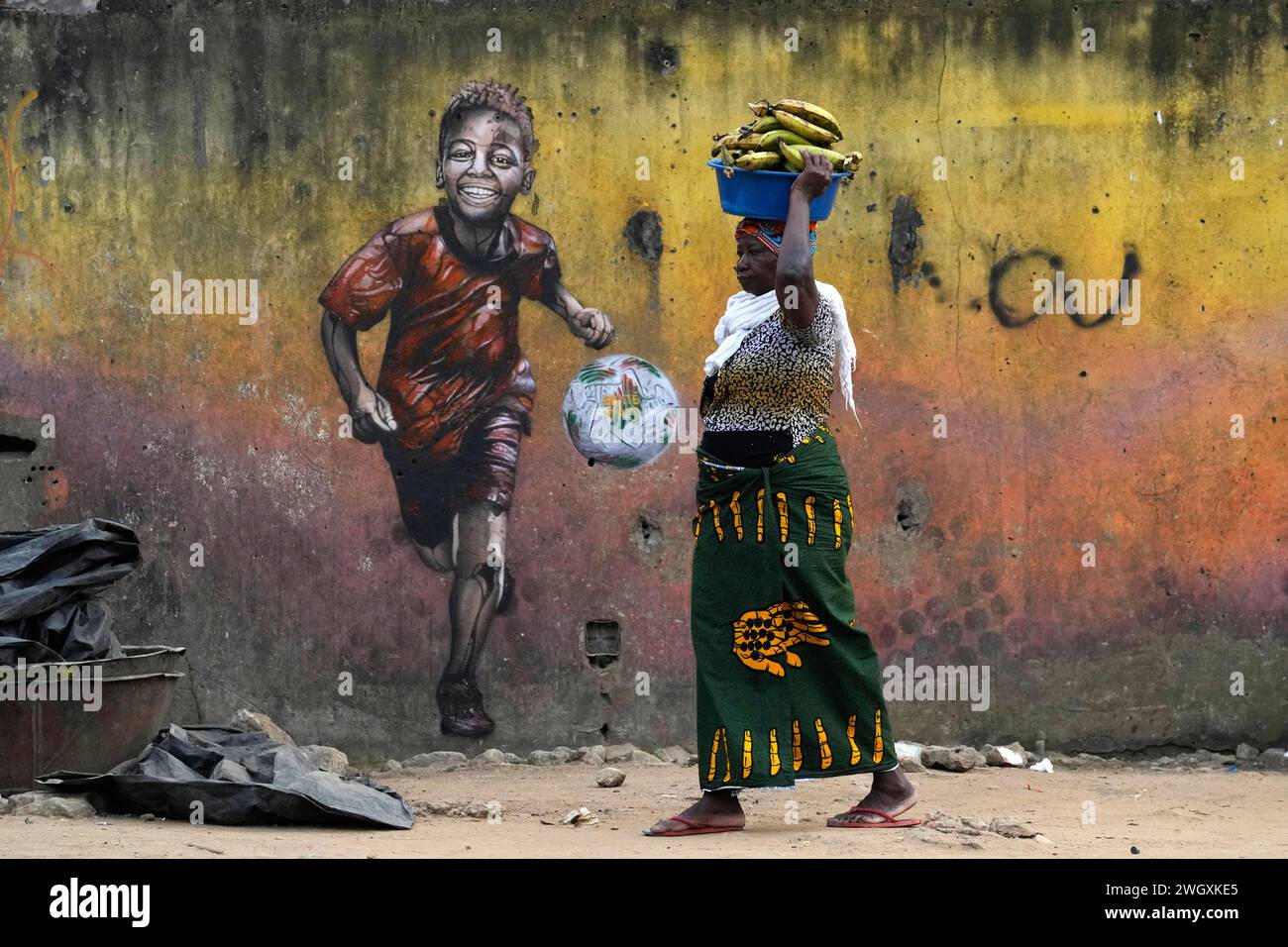 A woman carrying on her head a bucket filled with bananas walks past a ...