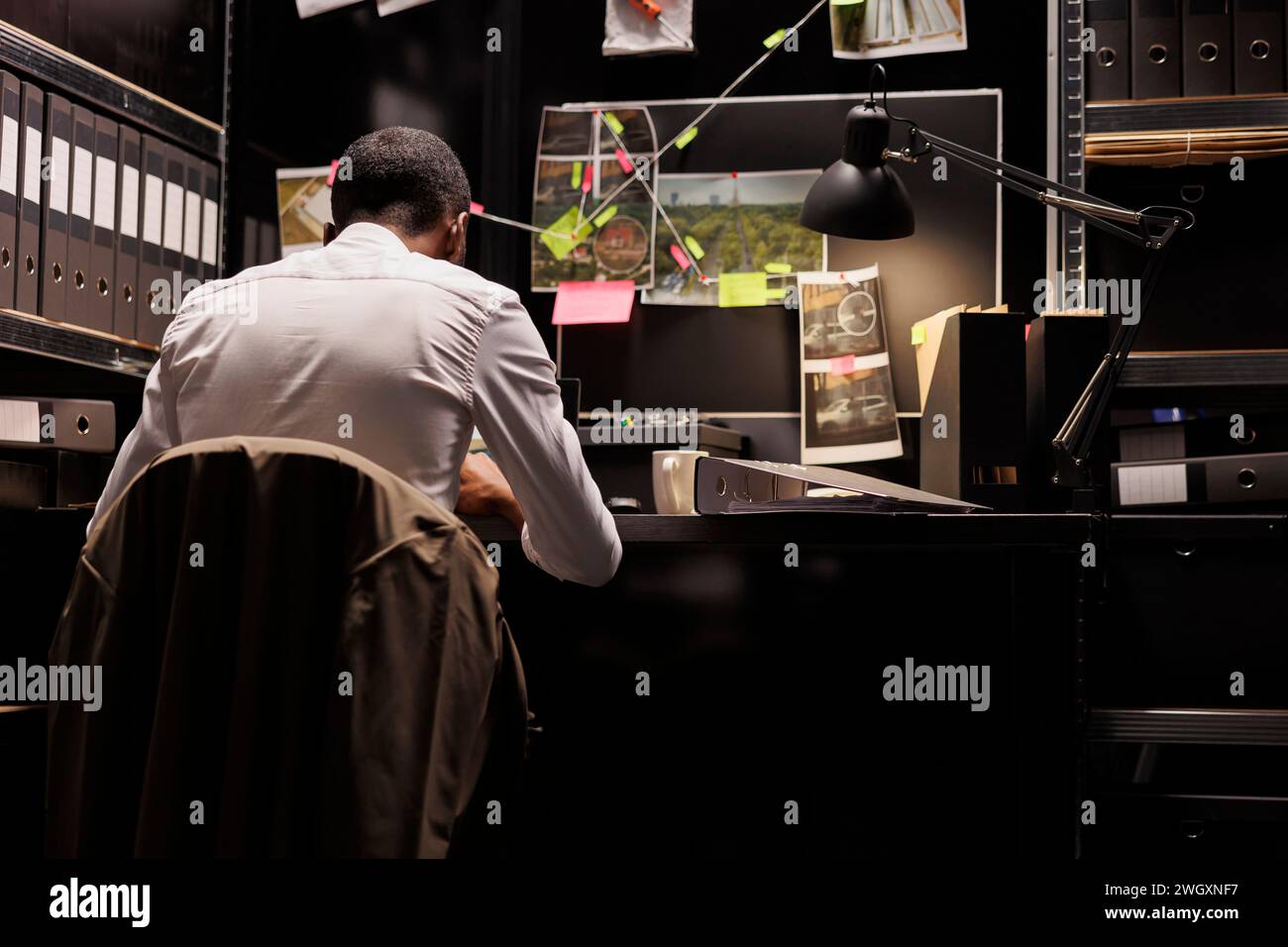 Detective sitting at workplace table and conducting investigation late ...