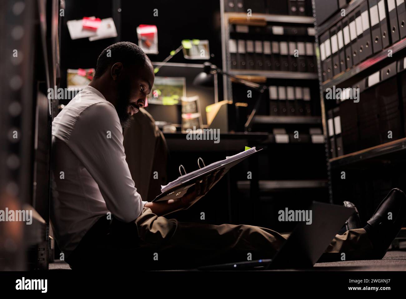 African american policeman reading crime case folder on floor in dark ...