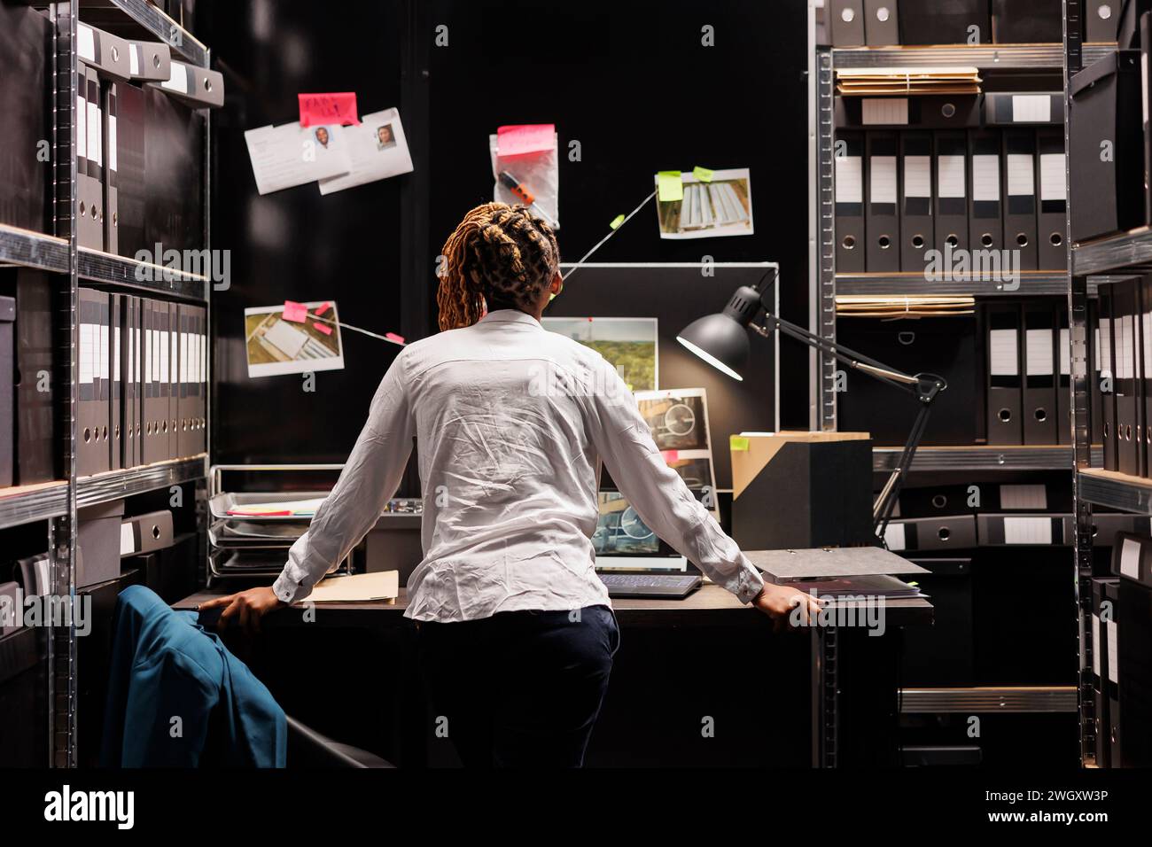 Policewoman standing near workplace and studying detective board ...