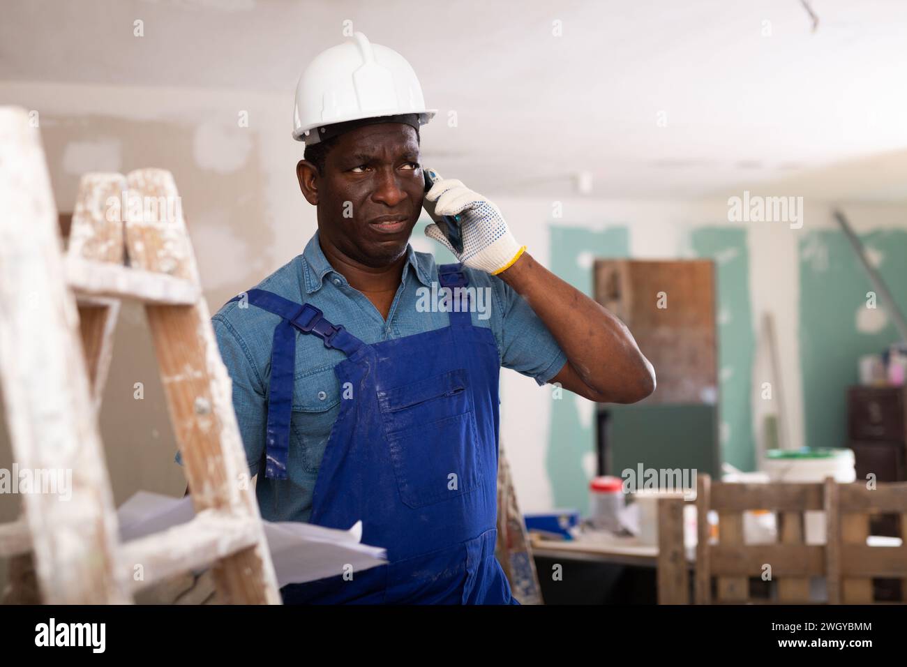 Worker in blue overalls communicates on a mobile phone in renovated ...