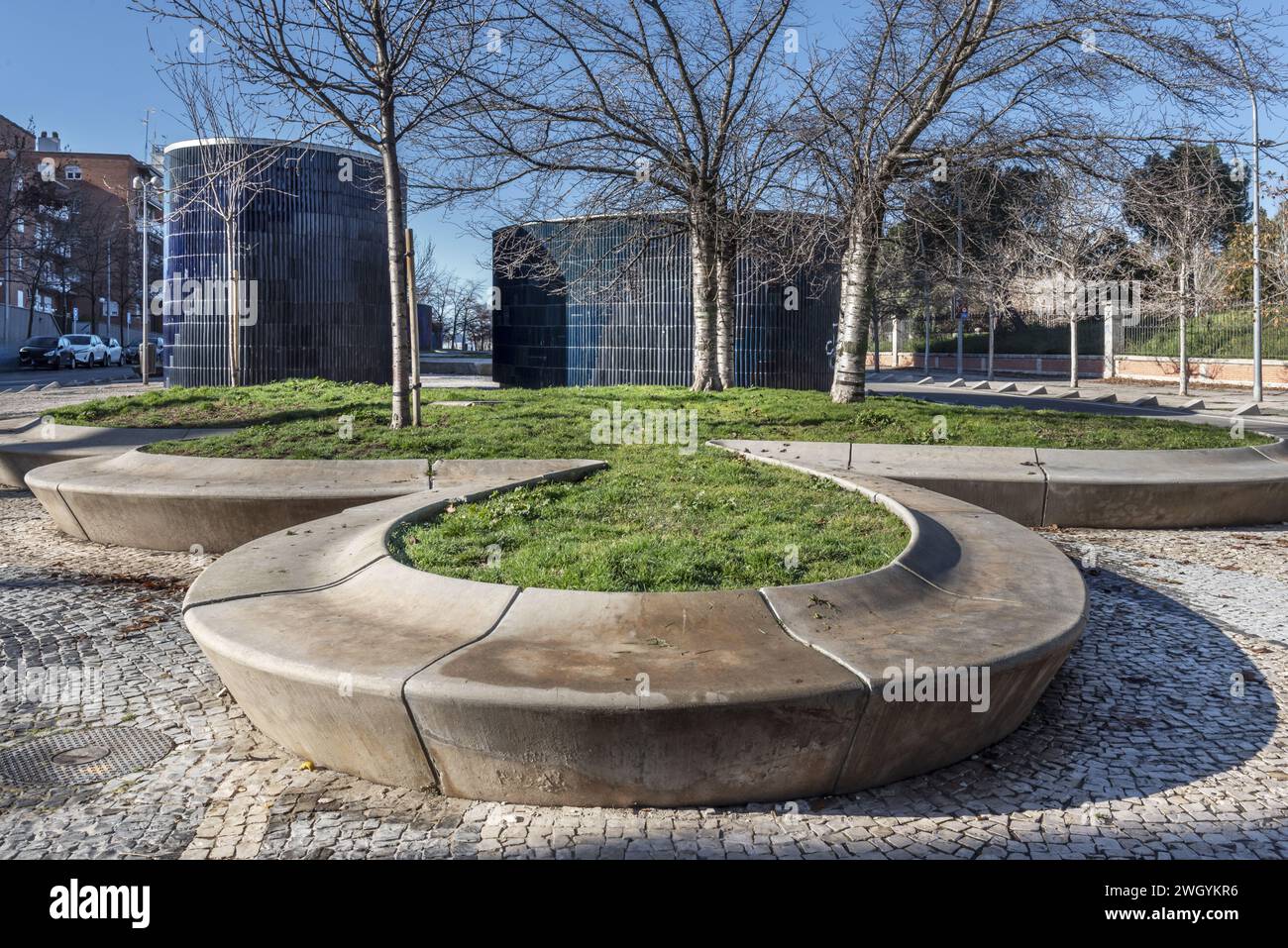 An urban park with circular stone seats and gardens with trees on top ...