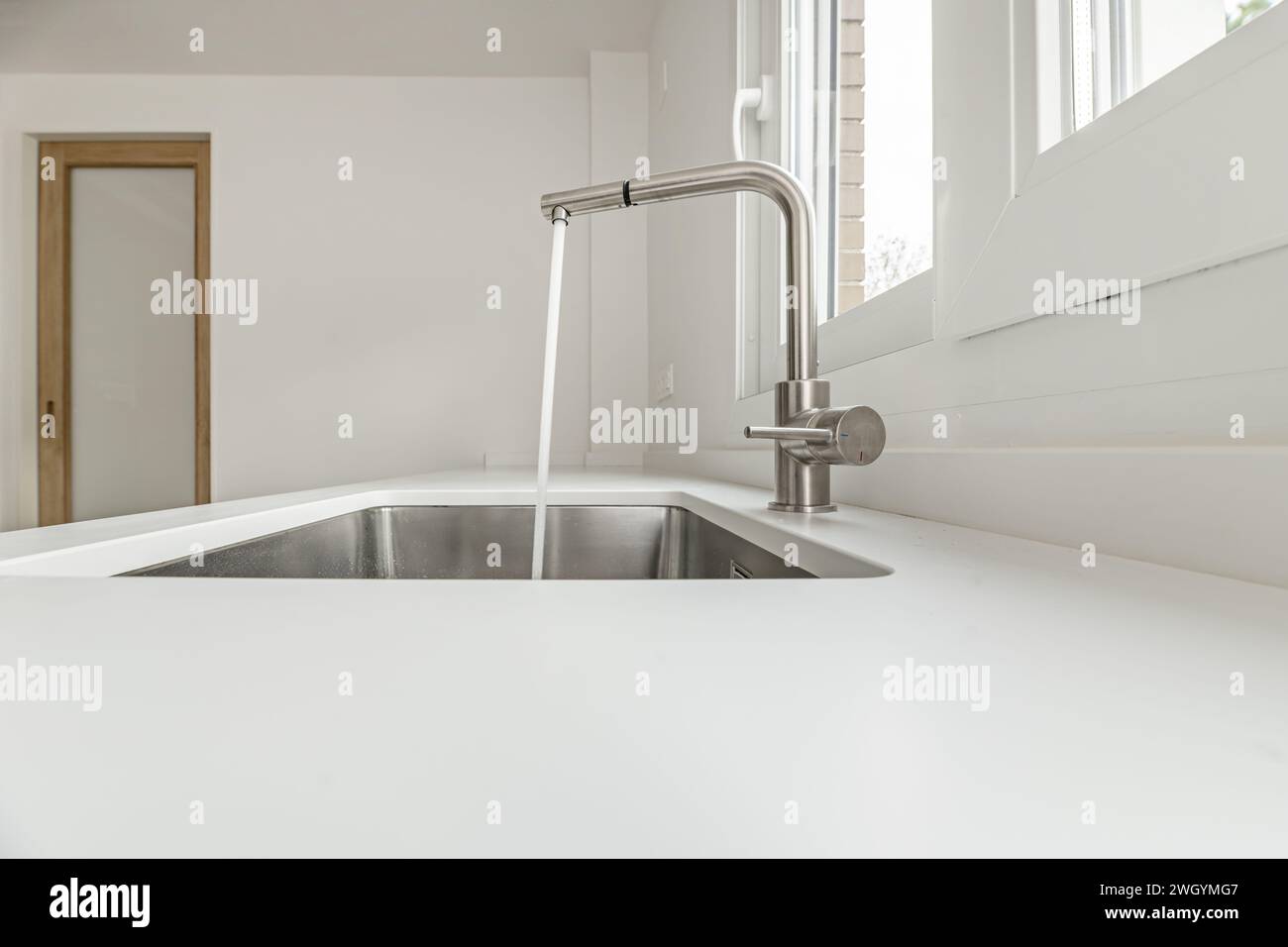 Stainless steel faucet and sink in a kitchen with white faux stone ...