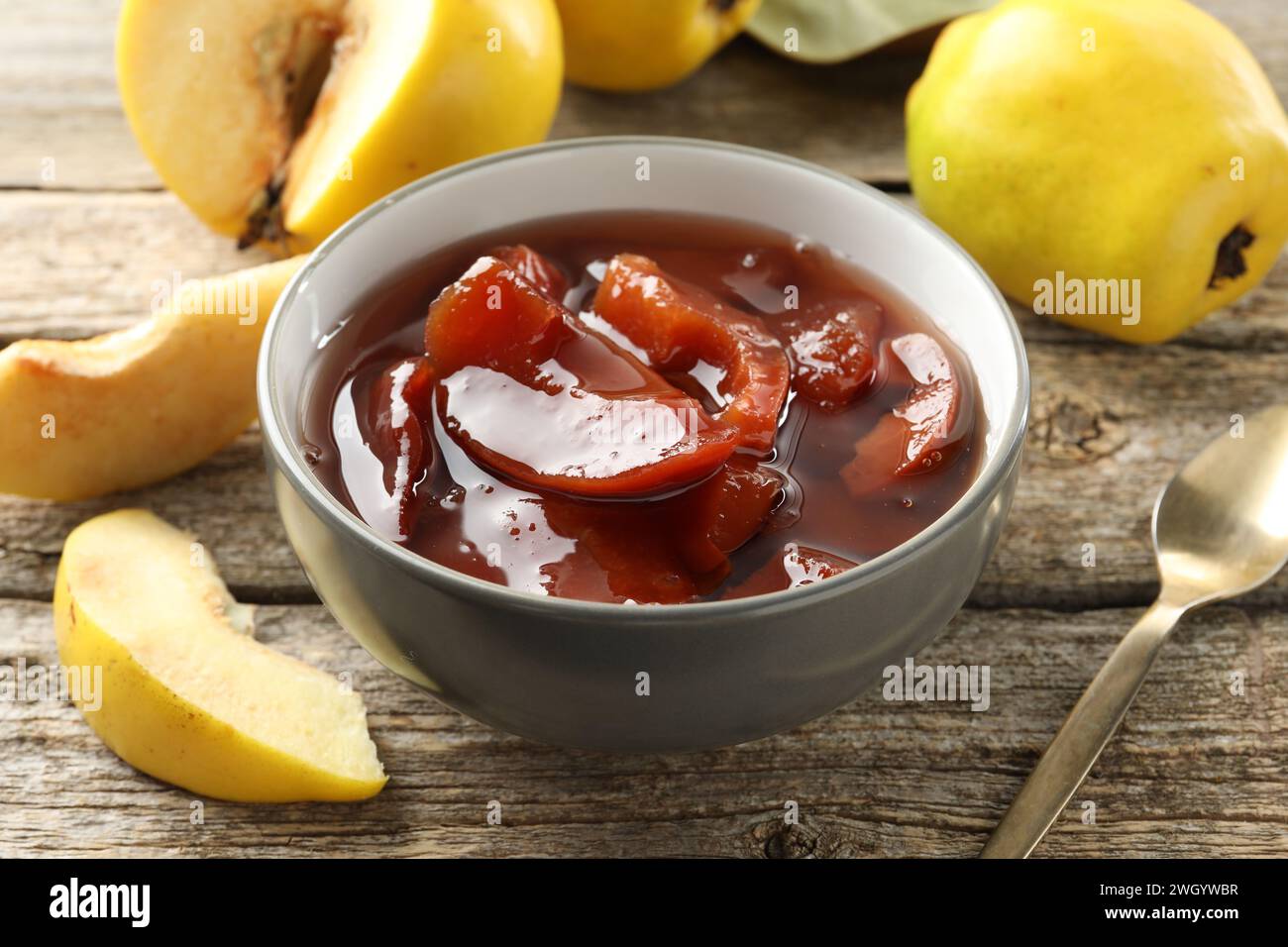Tasty homemade quince jam in bowl, spoon and fruits on wooden table ...