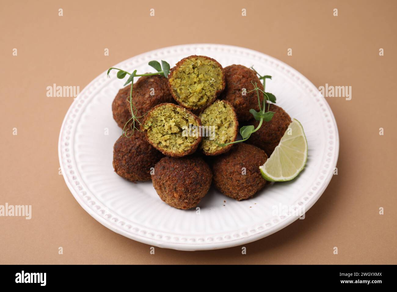 Delicious falafel balls, lime slice and microgreens on pale brown ...
