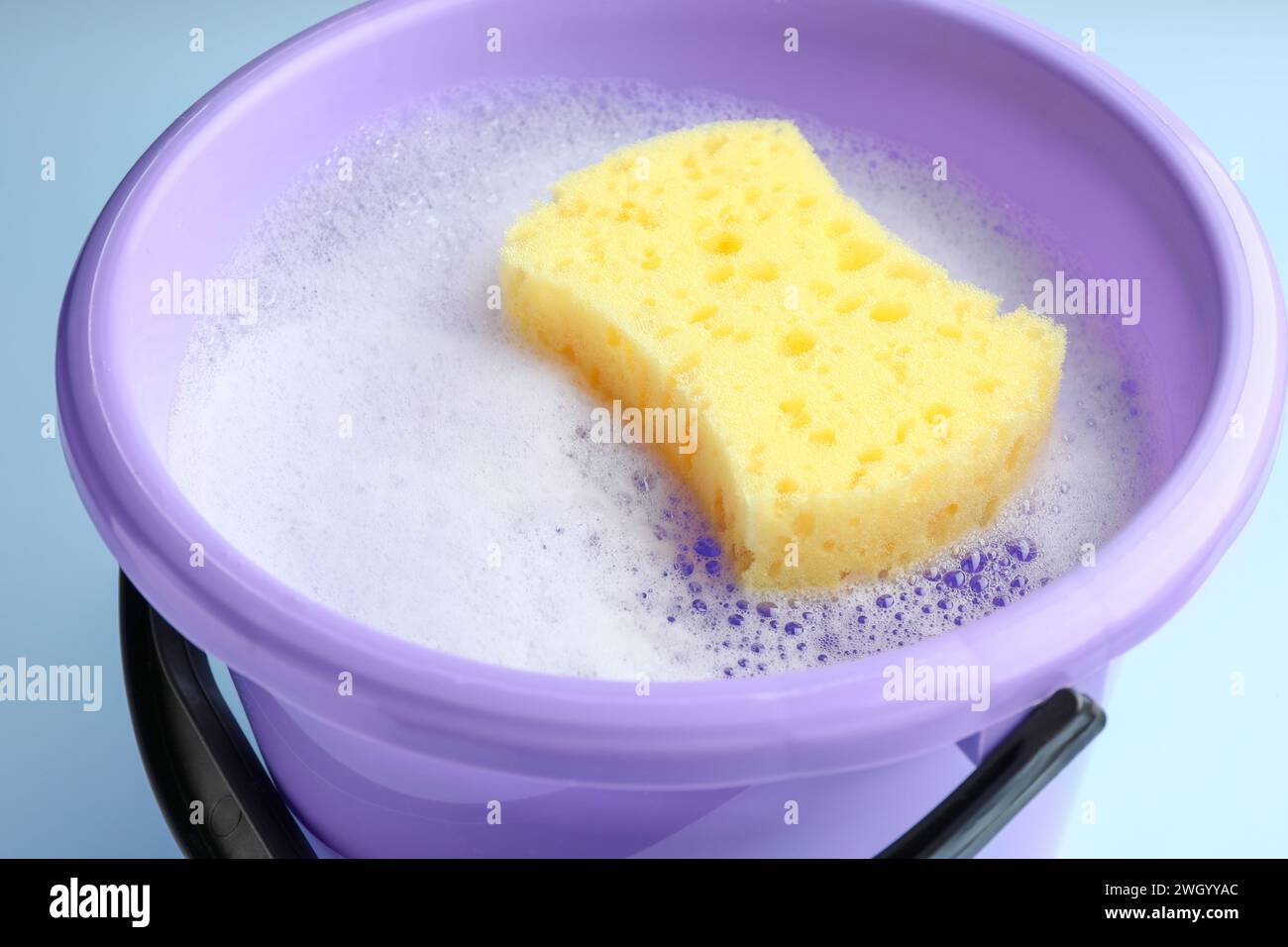 Bucket with foam and sponge on light blue background, closeup Stock ...