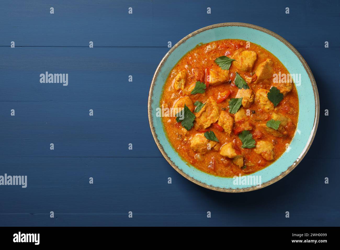 Delicious chicken curry on blue wooden table, top view. Space for text ...