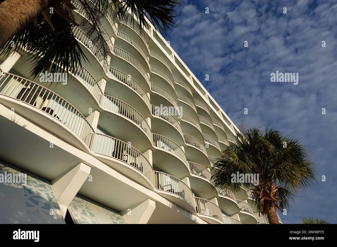 Symmetrical white hotel with balconies, surrounded by palm trees under ...