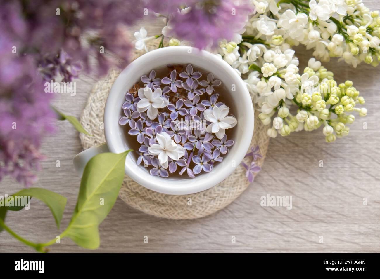 Tasty black tea in white cup on windowsill with aromatic lilac flowers ...