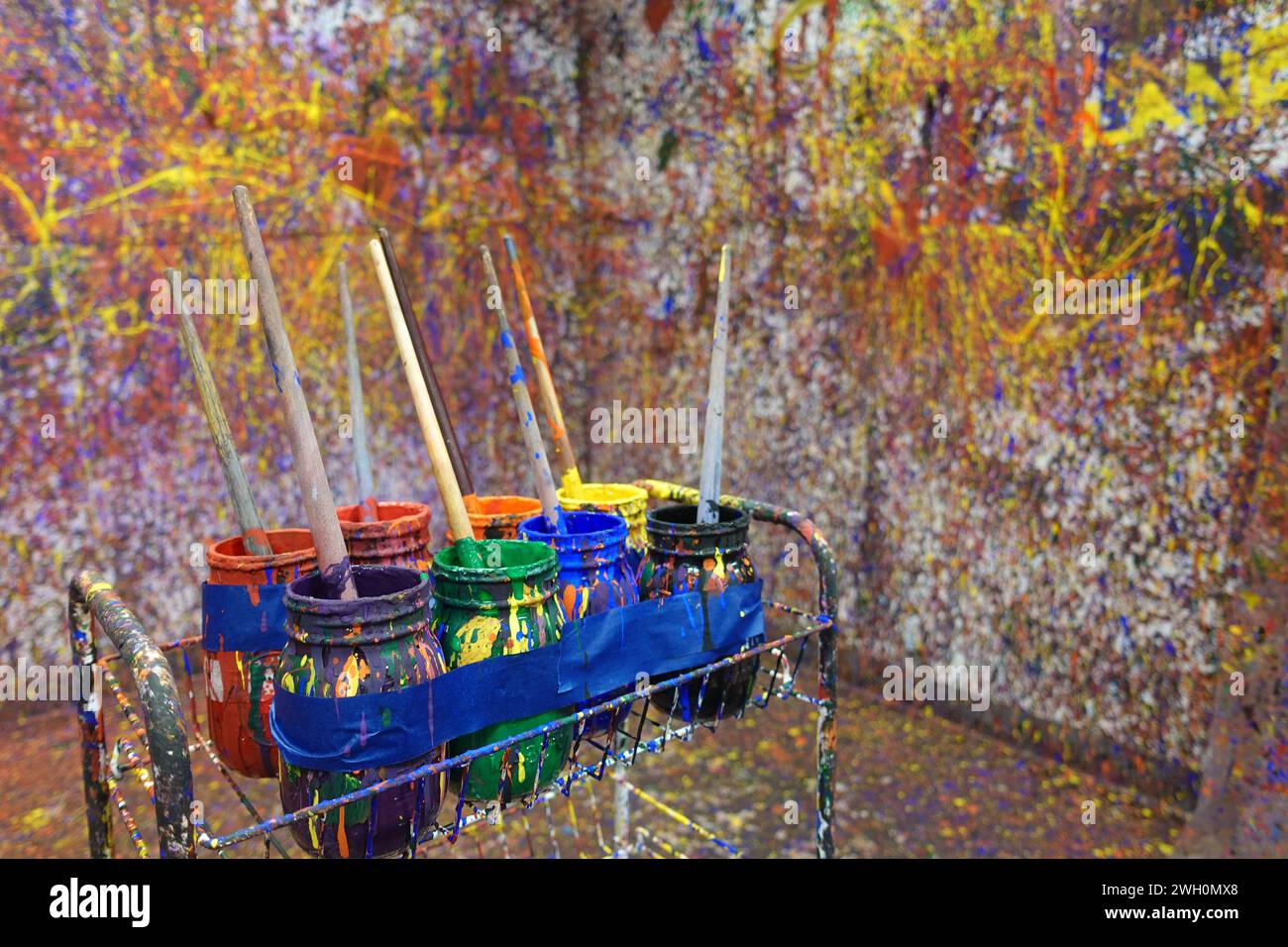 Various paint colors and brushes against a wall of splashed paints ...
