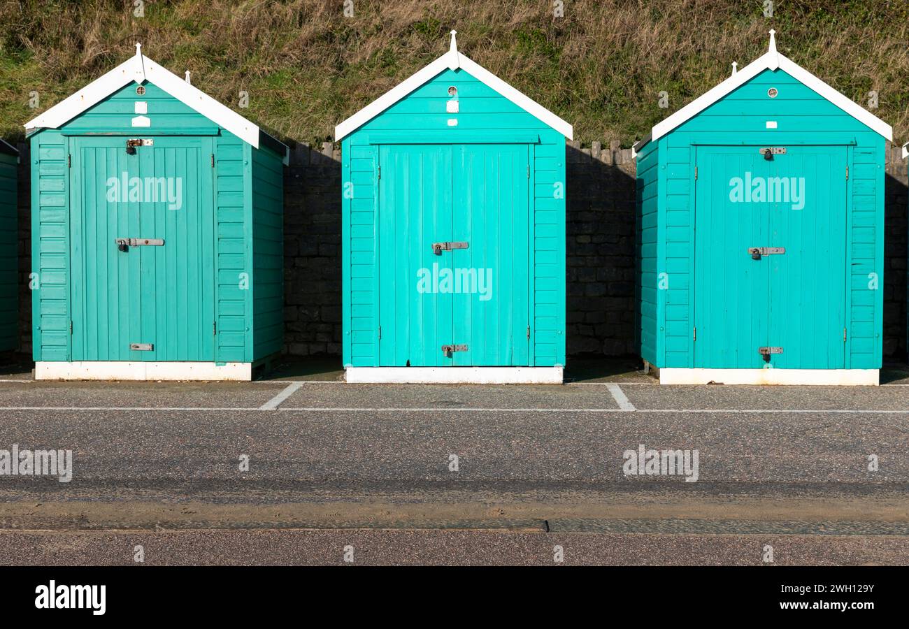 Three beach huts in shades of aqua blue on a promenade in Dorset. Taken ...