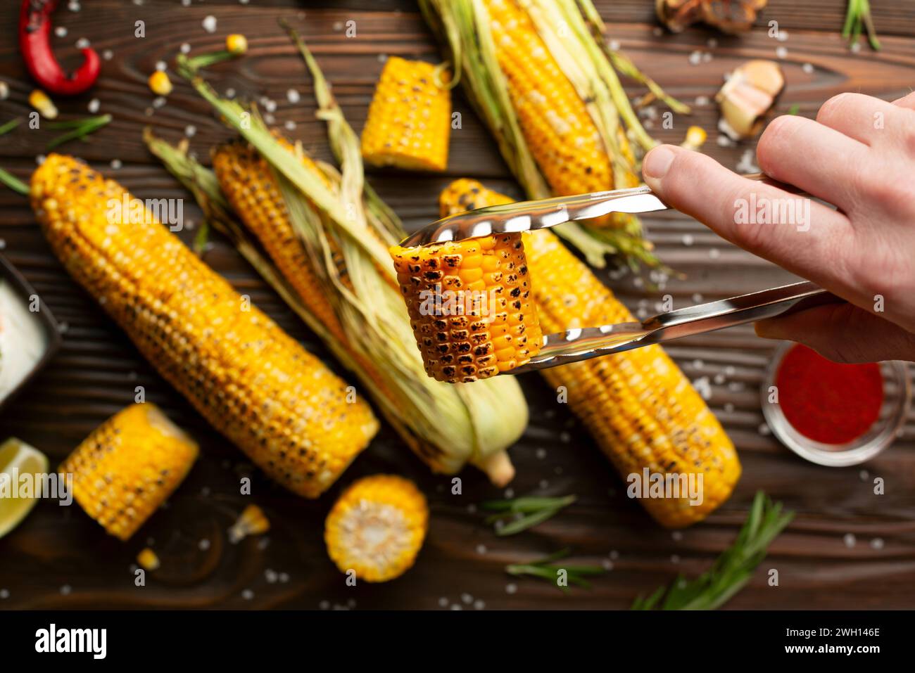 Kitchen tongs with grilled corn on the cob pieces in caucasian hands on ...