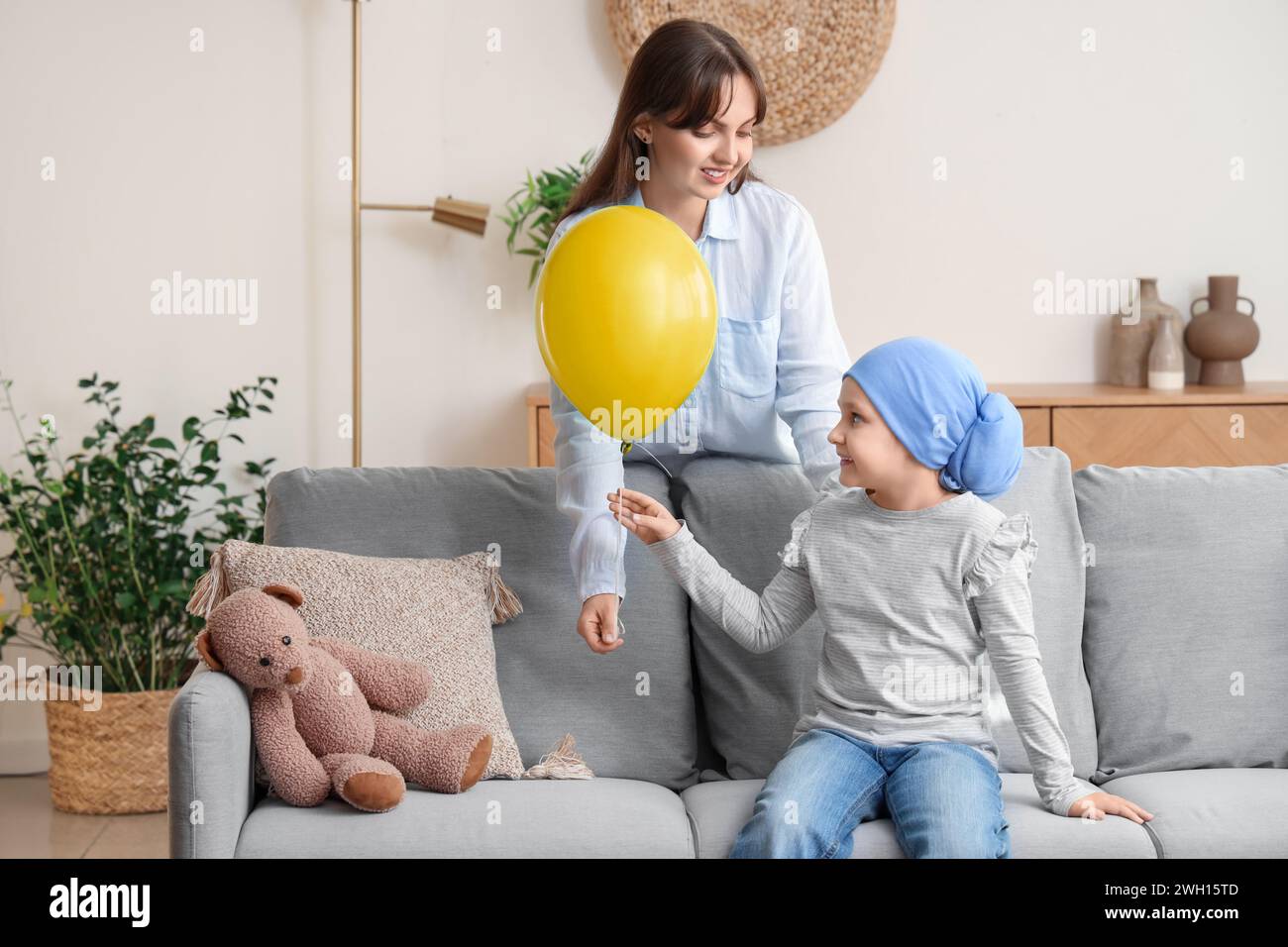 Little girl after chemotherapy with blue balloon and her mother at home ...
