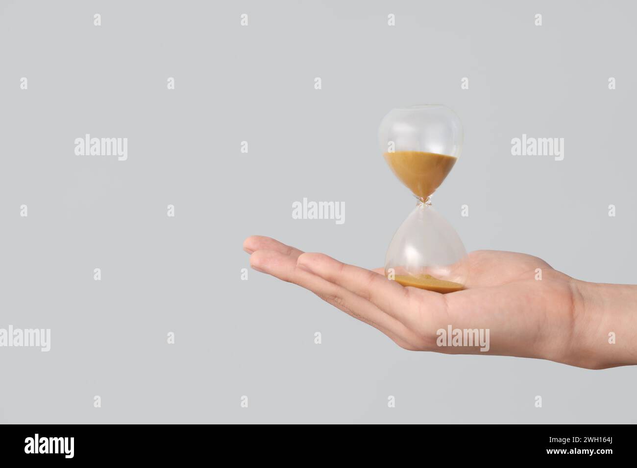 Female hand holding hourglass on grey background Stock Photo - Alamy