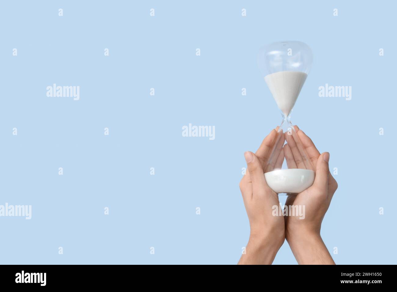 Female hands holding hourglass on blue background Stock Photo - Alamy