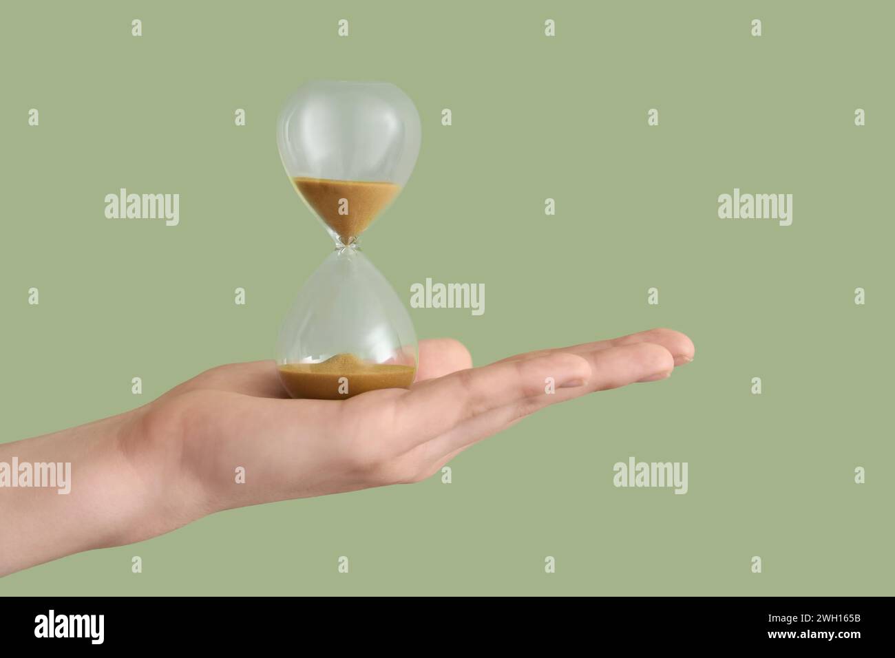 Female hand holding hourglass on green background Stock Photo - Alamy