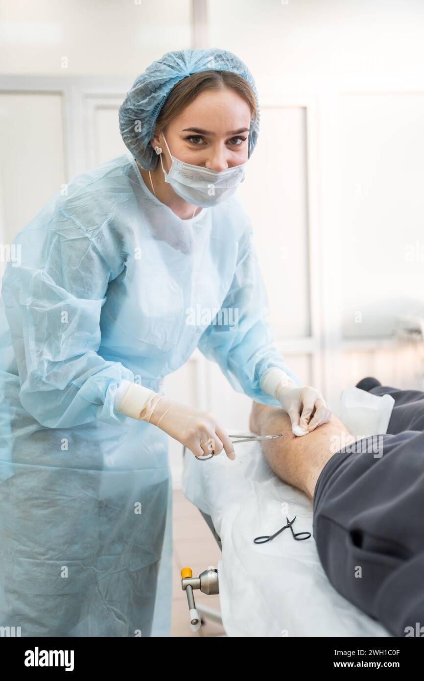 Smiling dermatologist surgeon stitching up a wound after skin surgery ...
