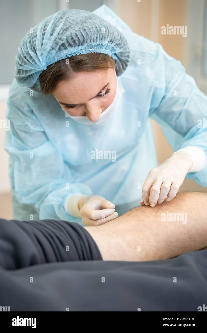 Portrait of dermatologist surgeon stitching up a wound after surgery ...